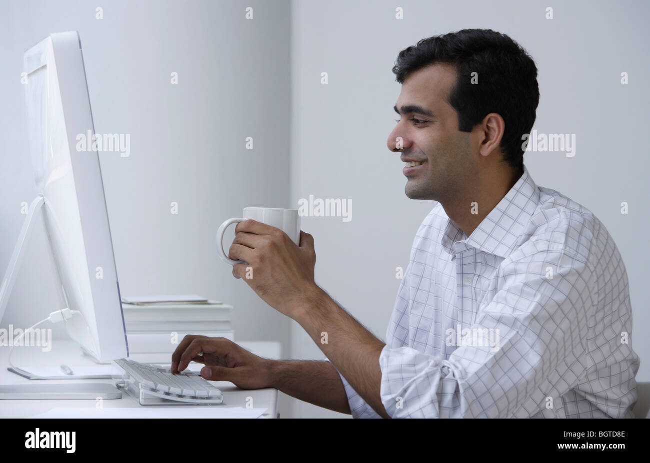 Indian man working on computer and drinking coffee Stock Photo - Alamy