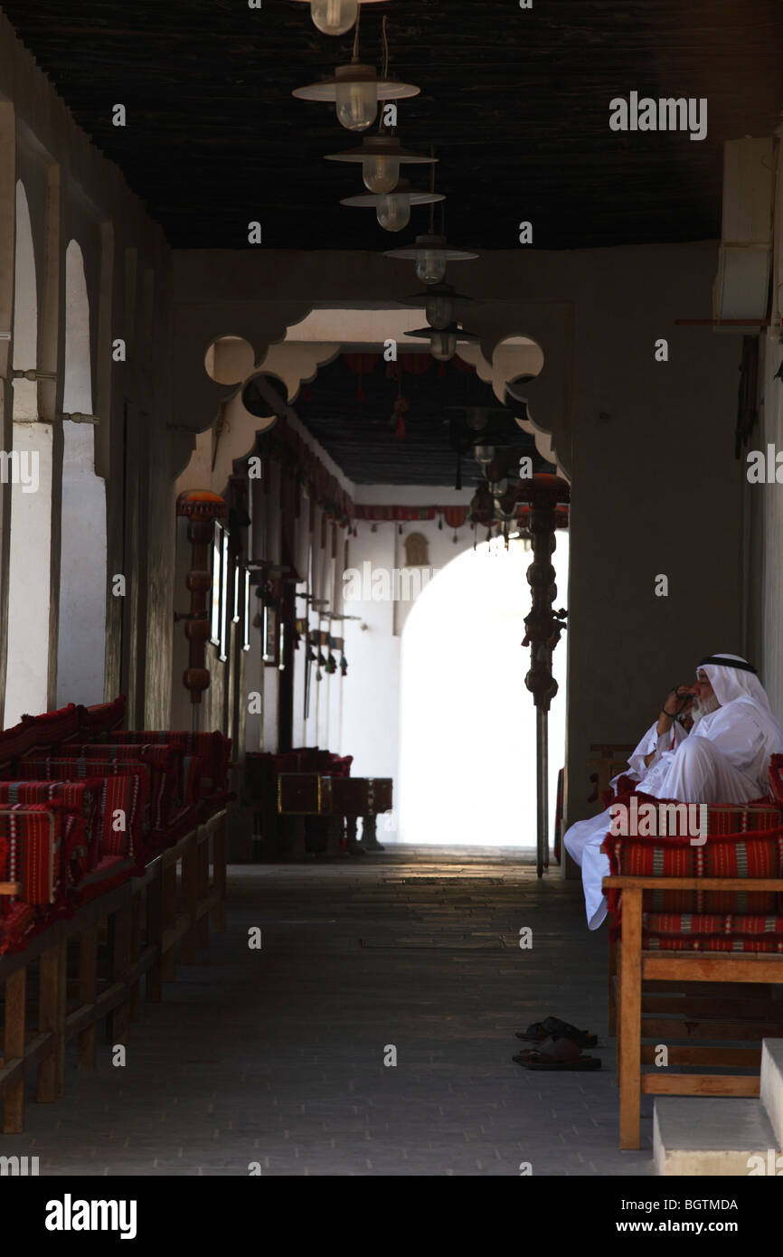 Qatari men (one barely visible) sitting on a bench in a portico outside ...