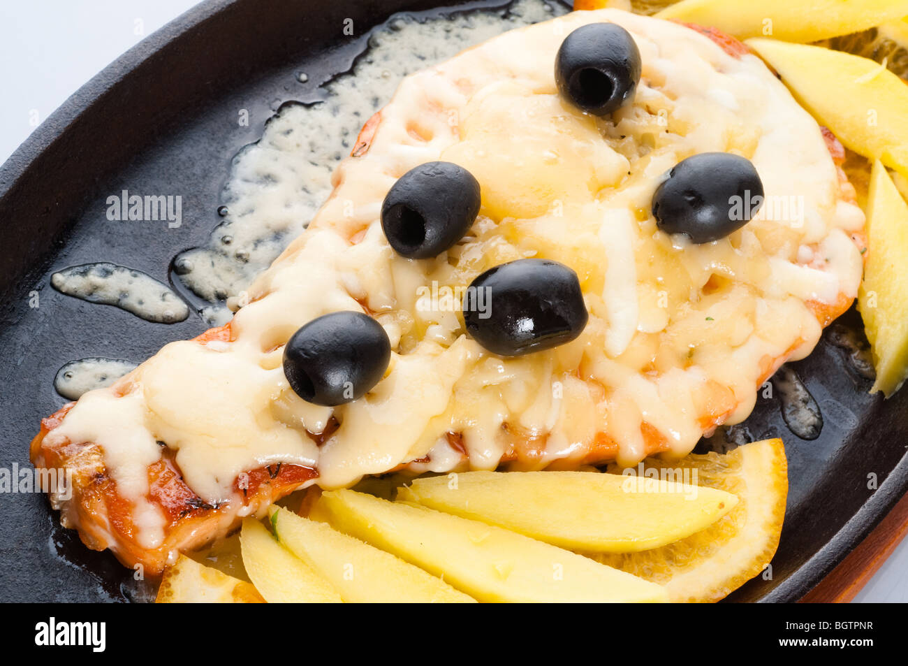 Fish in cheese sauce with olives on a frying pan Stock Photo - Alamy