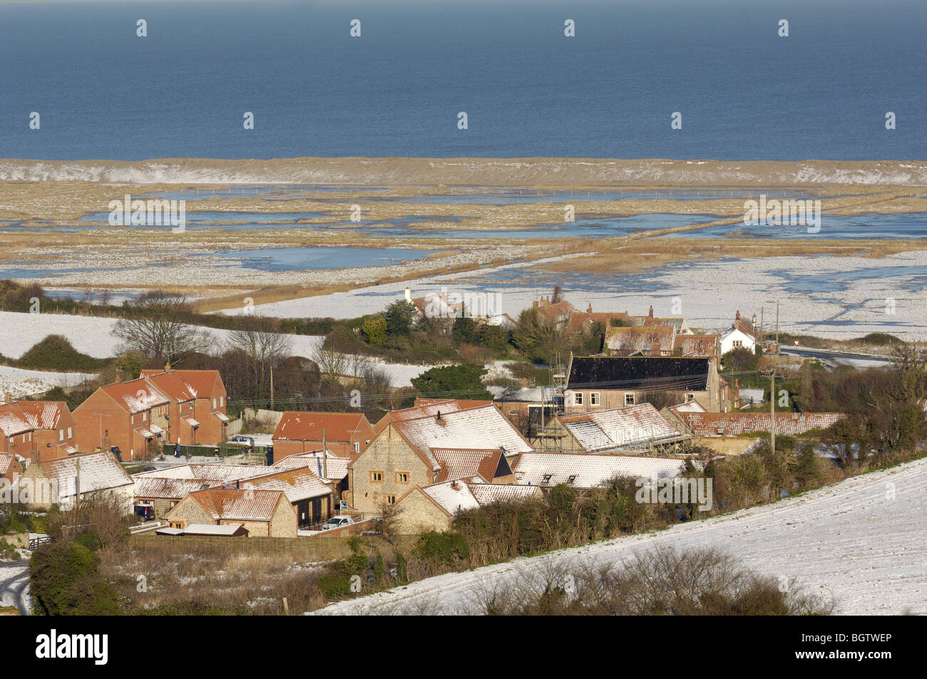 Salthouse village with snow covered roofs and snowy salt marsh, Norfolk ...