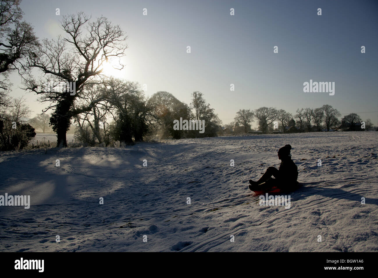 Picturesque silhouetted winter scene of a boy sledging in a snowy ...
