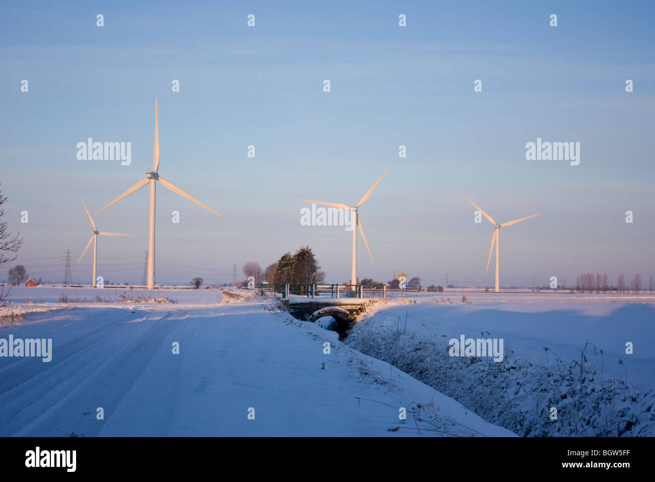 Sunlit wind farm in a flat snowy fenland landscape against a cold blue ...