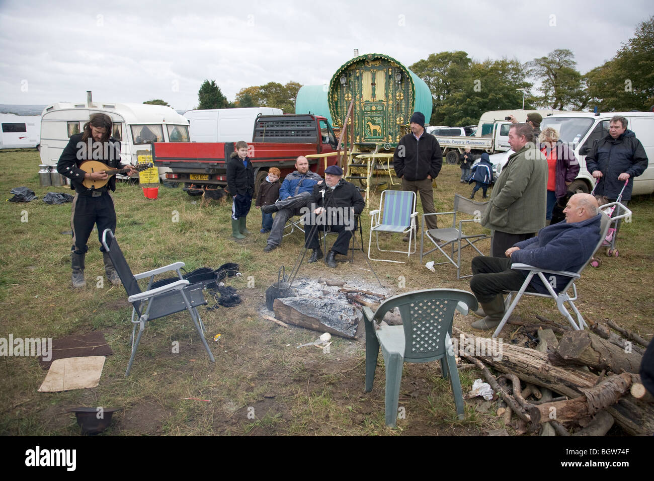 People gathered around a campfire while a man plays a mandolin, at Stow ...