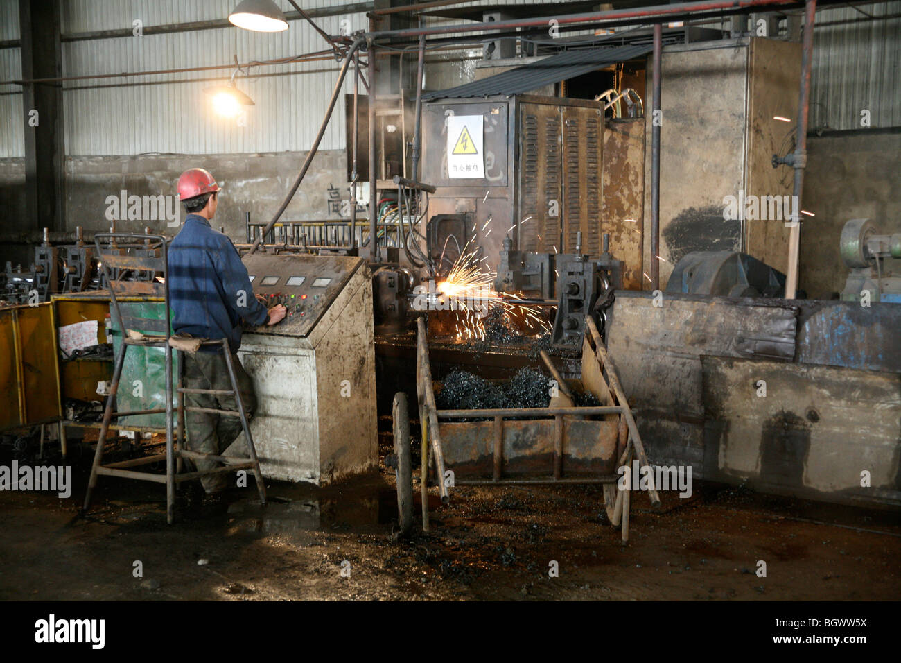 Chinese worker welding steel into a tube, wheelbarrow in foreground ...