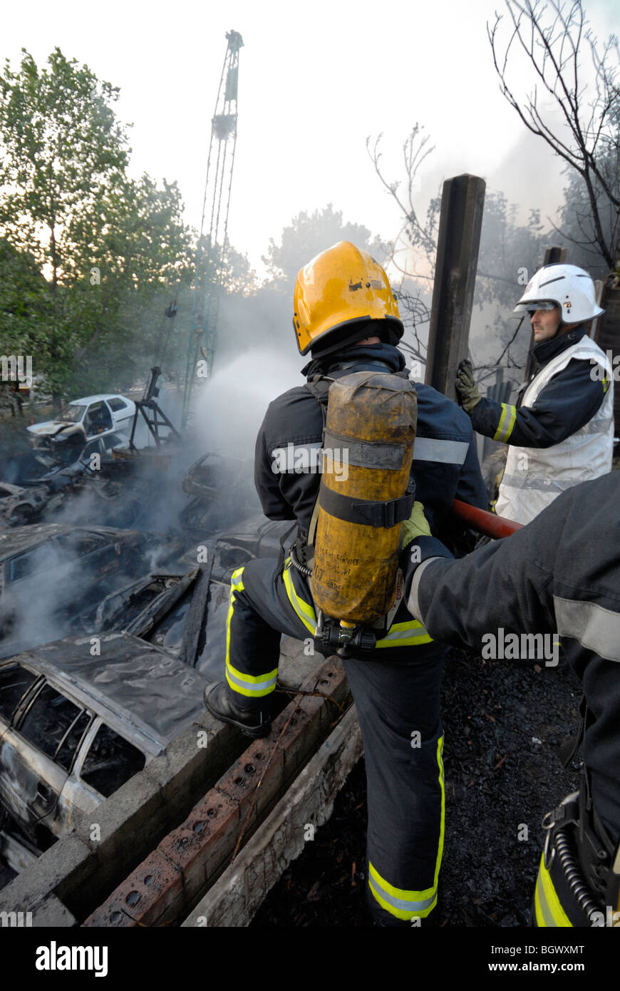 Firemen uses hose at scrapyard car fire Stock Photo - Alamy