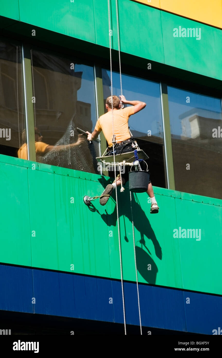 Close-up of one office Window cleaner suspended high up in a seat ...