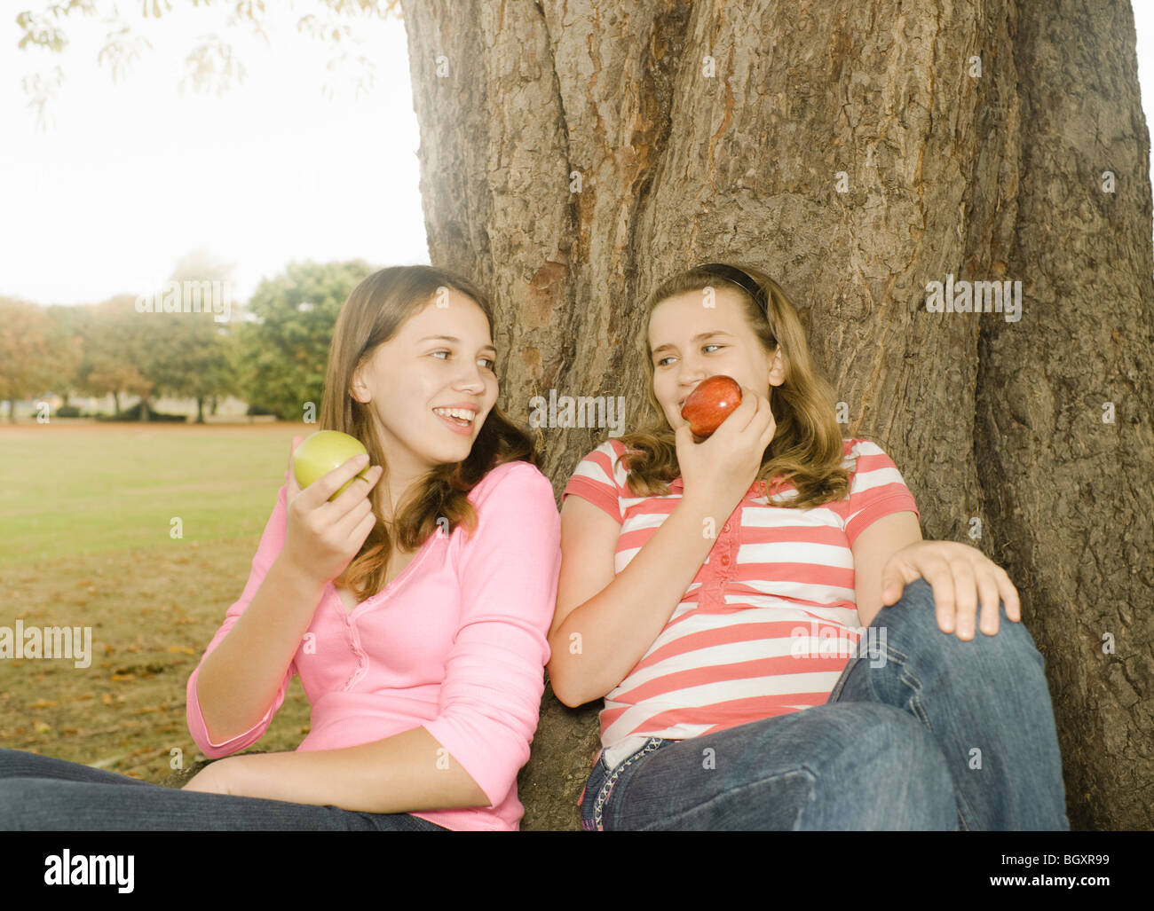 Girls eating apples against tree Stock Photo - Alamy