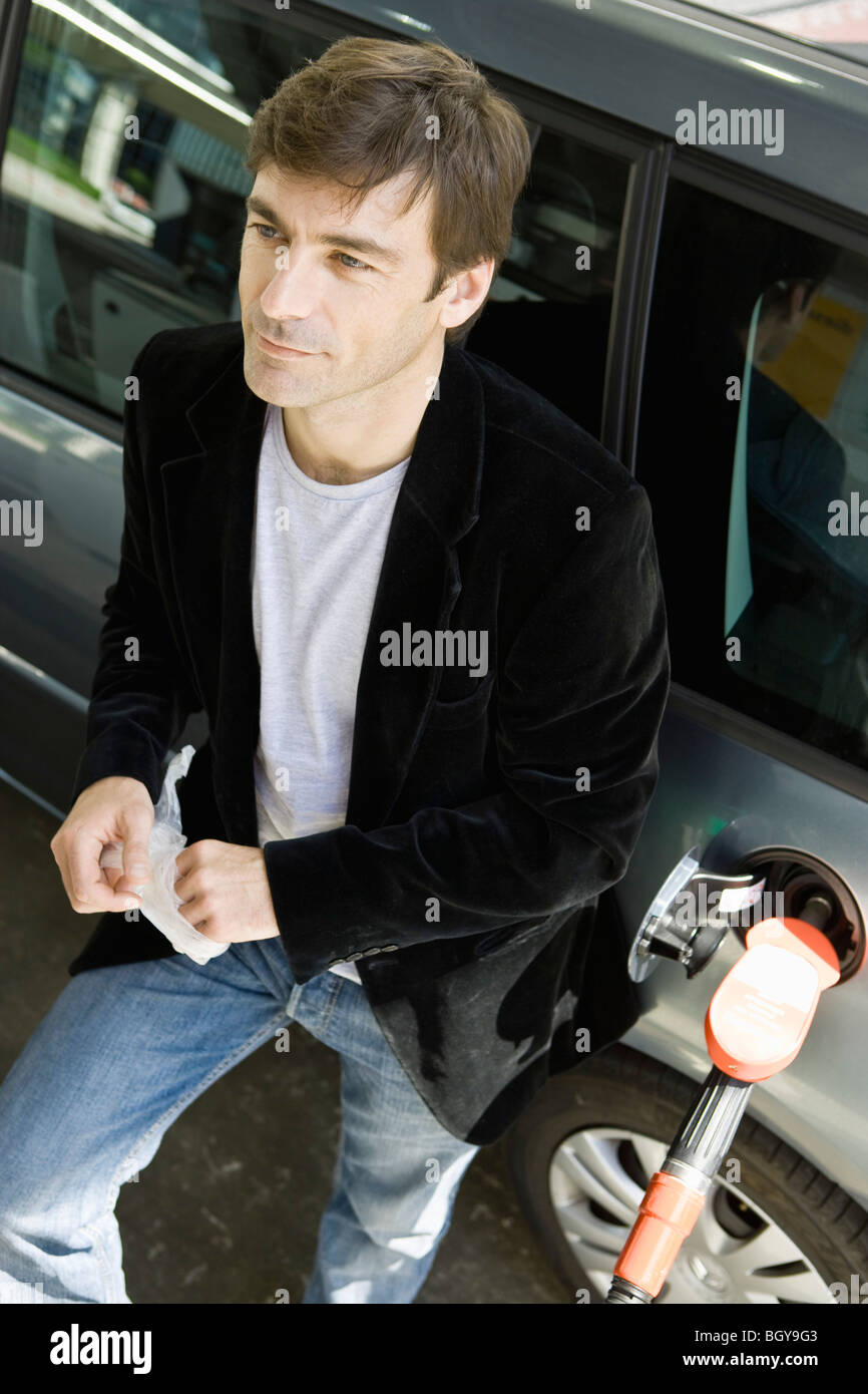 Man At Gas Station Leaning Against Car Waiting For Gas Tank To Fill