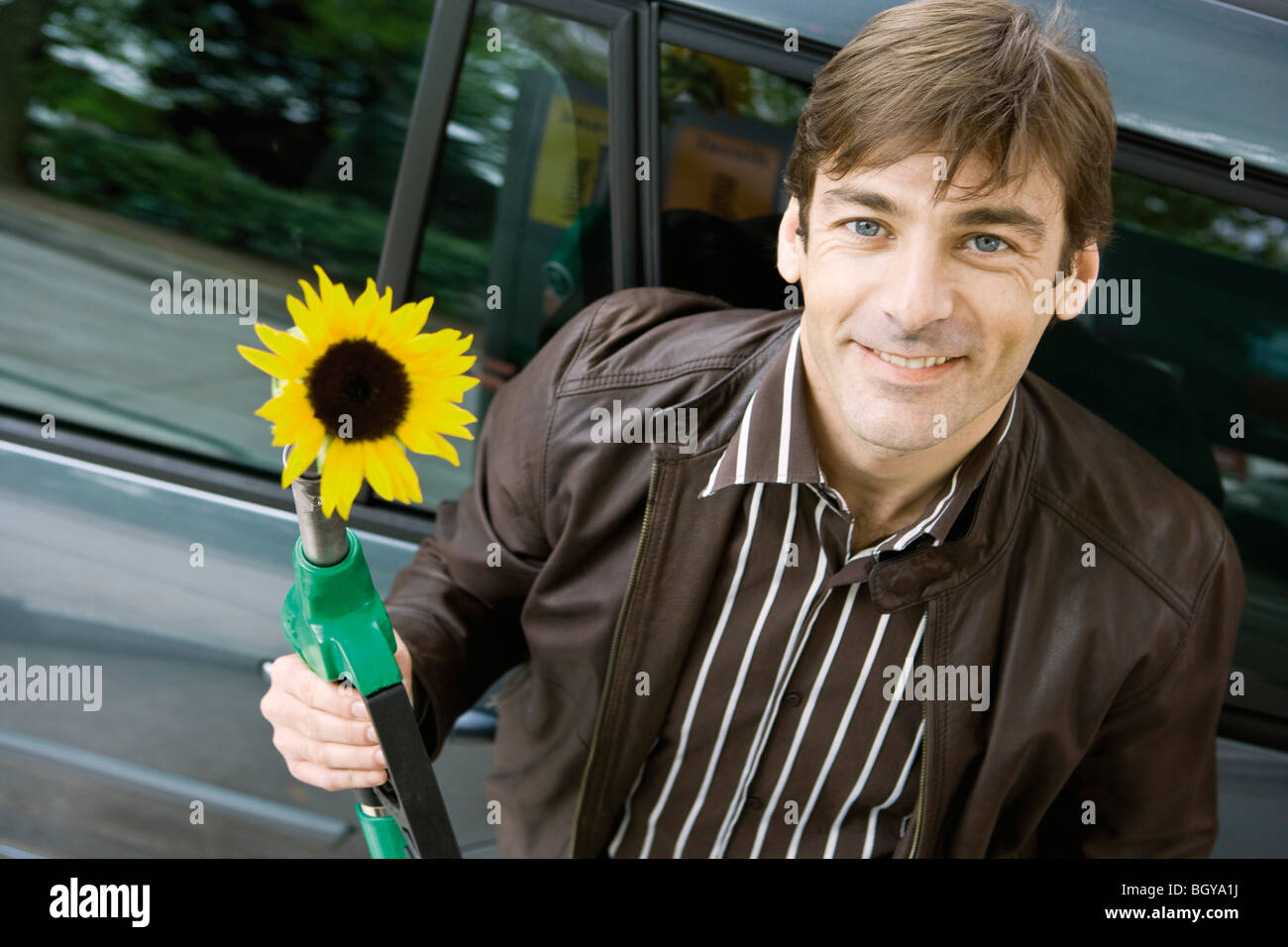 Man at gas station holding gas nozzle with sunflower emerging from end ...