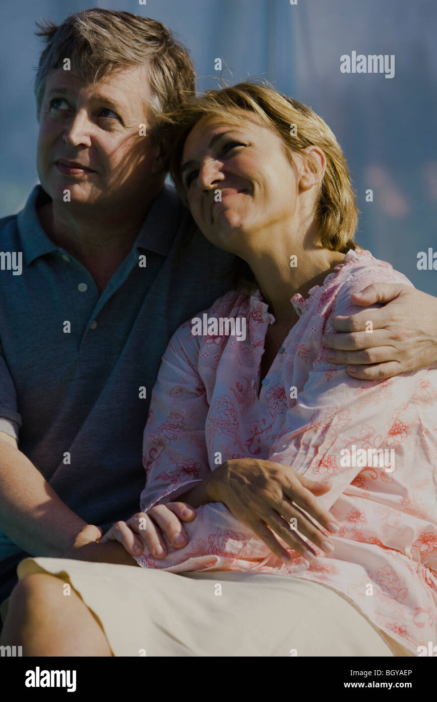Mature couple sitting together outdoors, man's arm around woman's ...