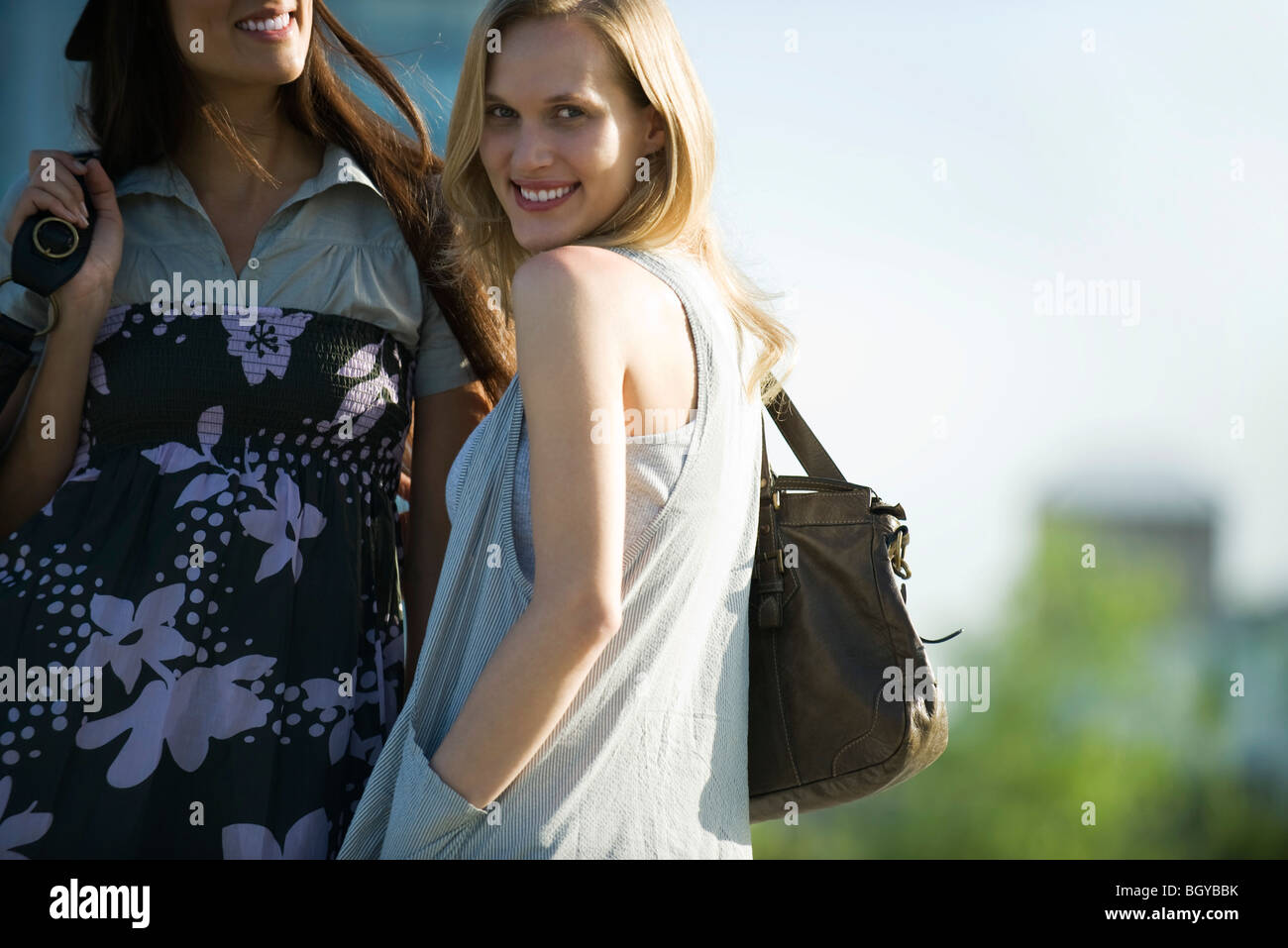 Two young women standing together, one smiling over shoulder at camera ...