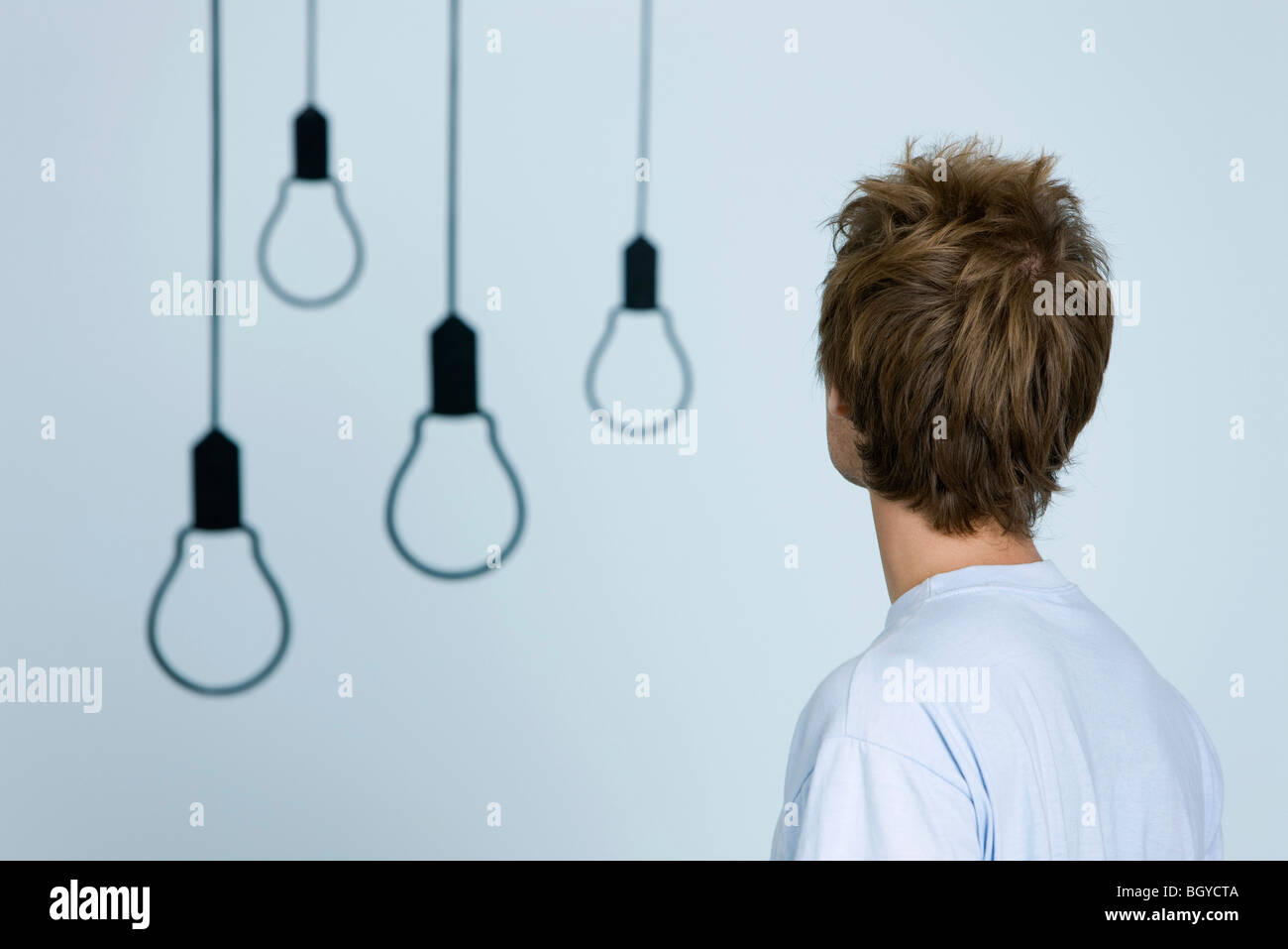 Young man looking at light bulb graphics on wall, rear view Stock Photo ...
