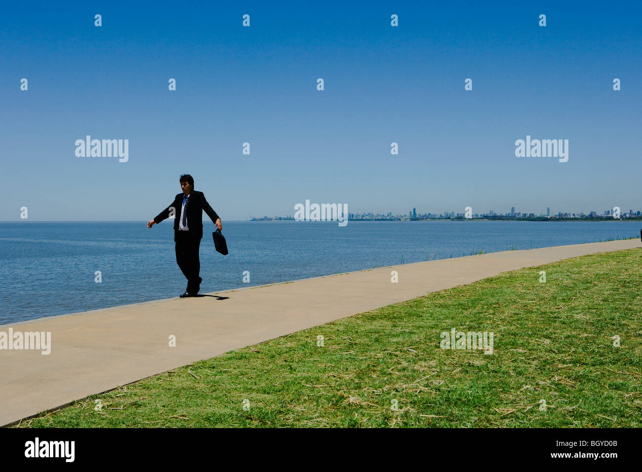 Businessman walking along edge of sidewalk along sea, arms out Stock ...