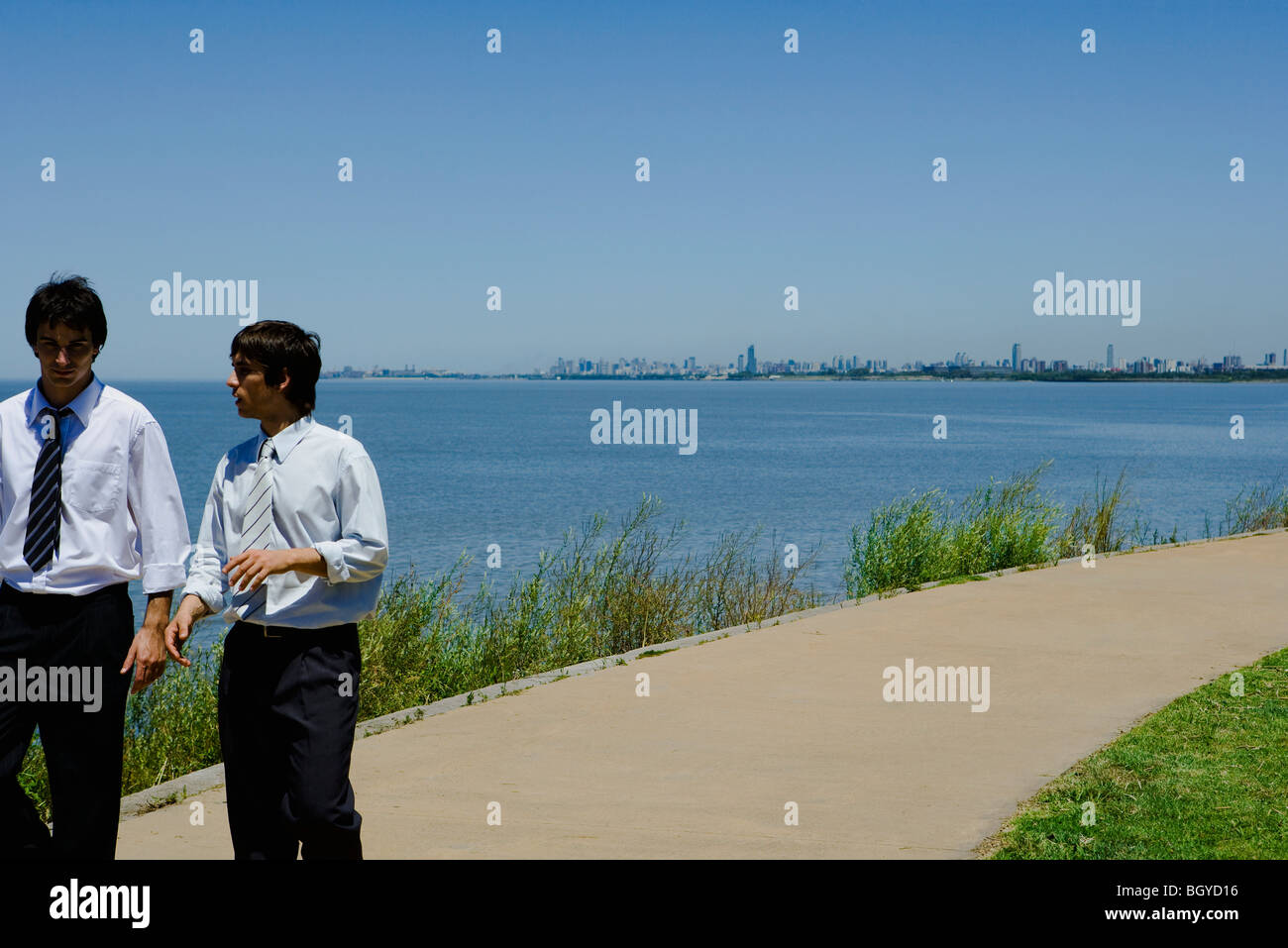 Young businessmen walking on sidewalk, talking, sea in background Stock ...