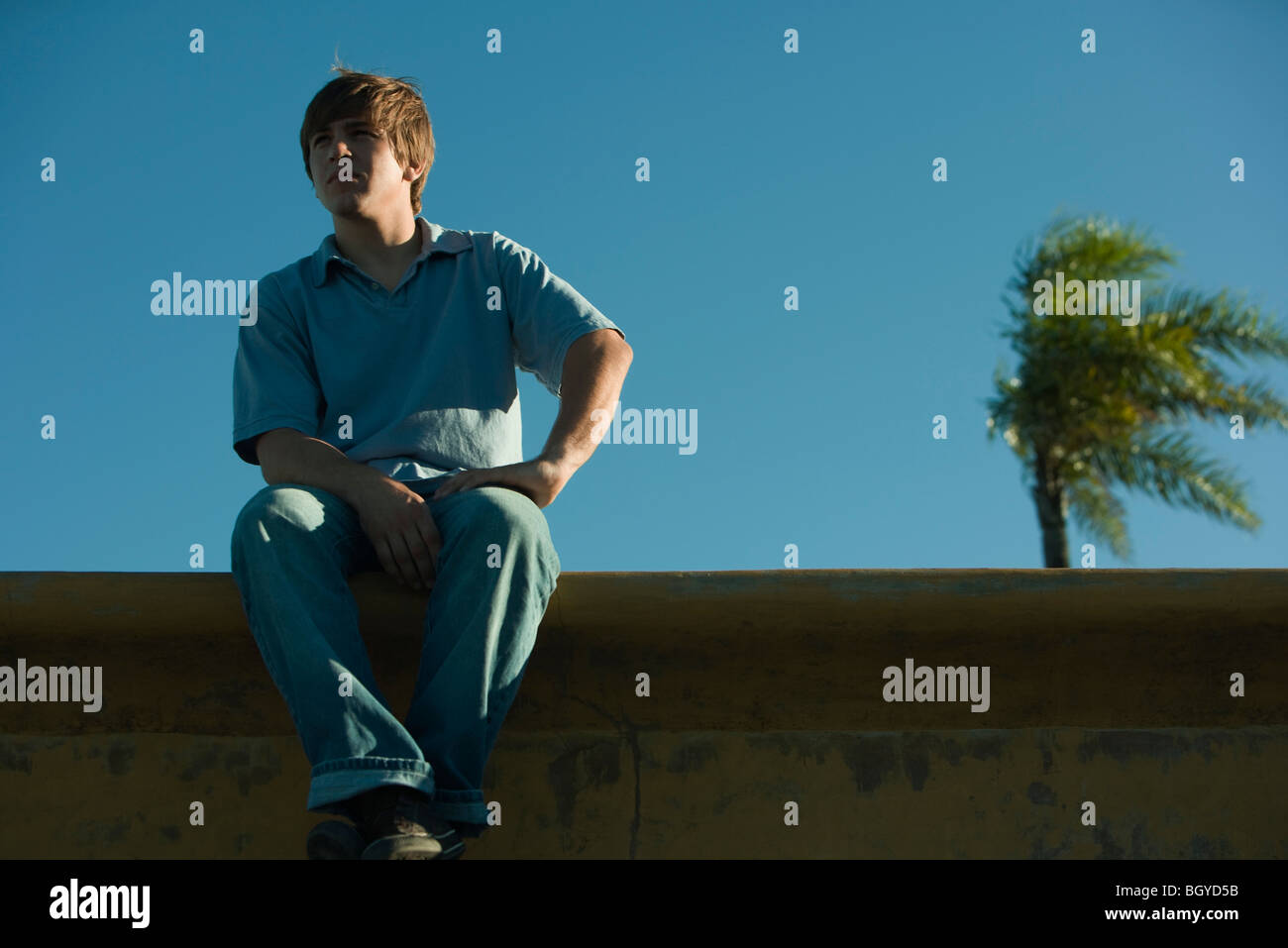 Young man sitting on ledge, looking away Stock Photo - Alamy