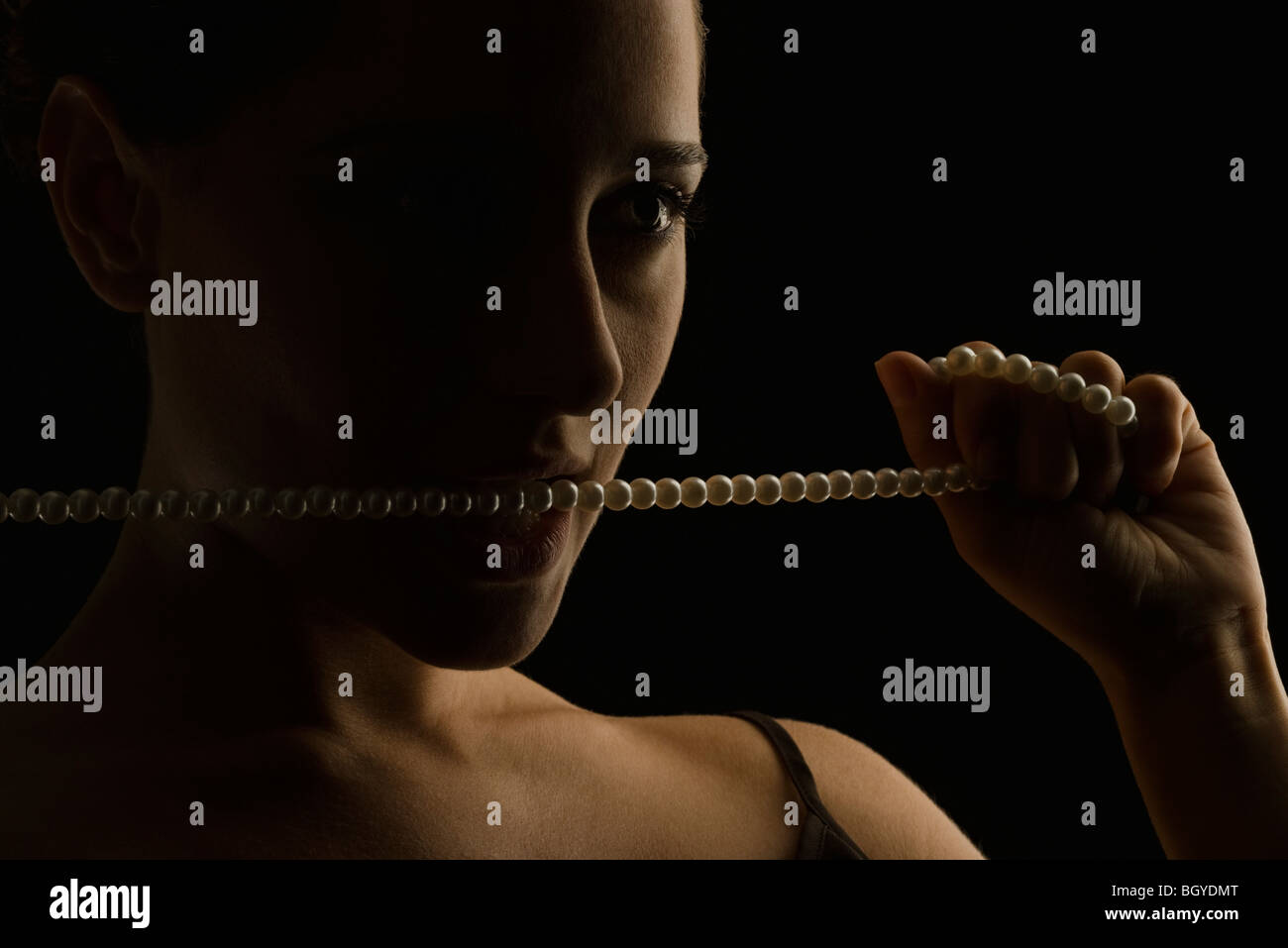 Woman holding string of pearls up to mouth, biting pearls, looking away ...