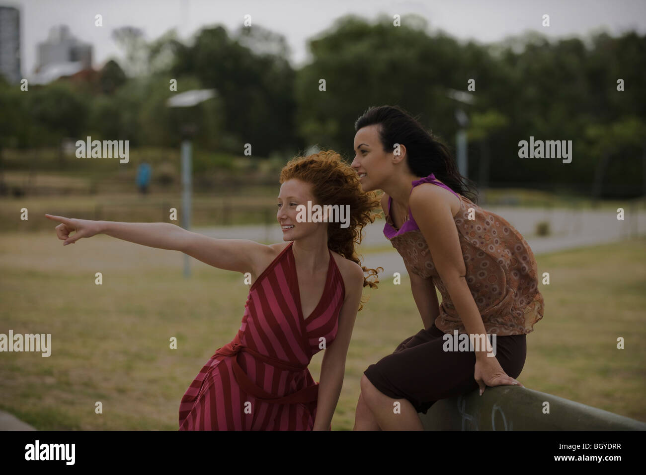 Two young women outside in park together, one pointing out of frame ...