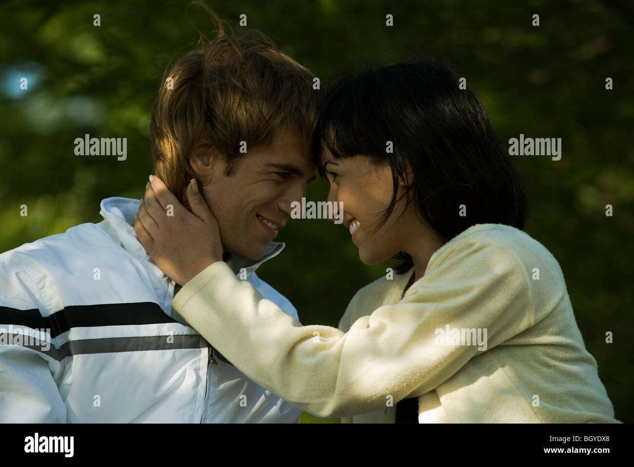 Young couple outdoors smiling at each other, foreheads pressed together ...