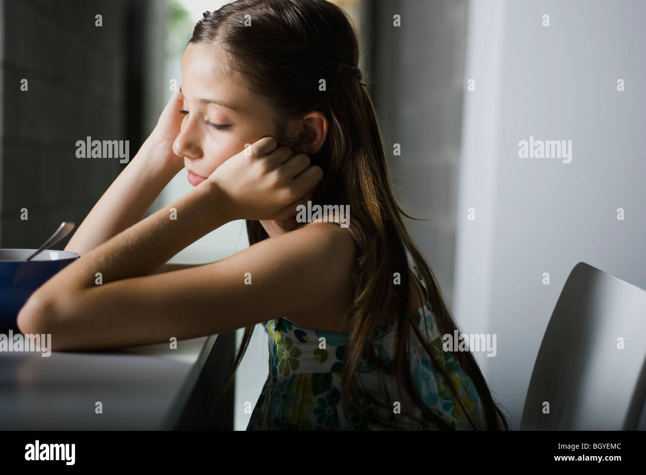Girl sitting at table with head in hands, looking sulkily at bowl in ...