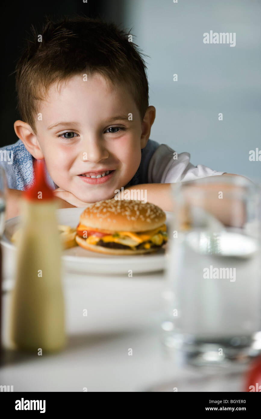 Little boy sitting at table with head resting on arms, looking at ...