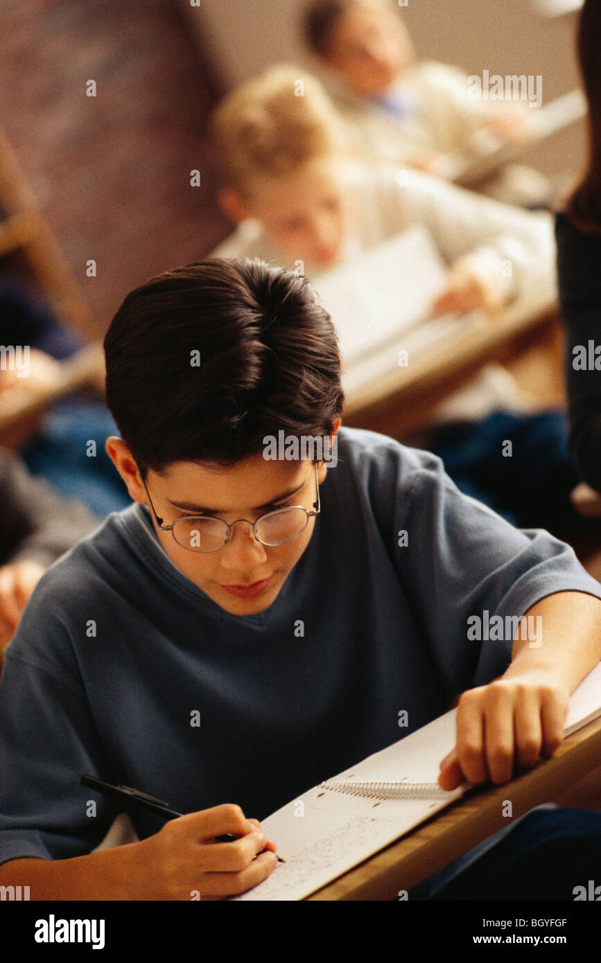 Student writing at desk in classroom Stock Photo - Alamy