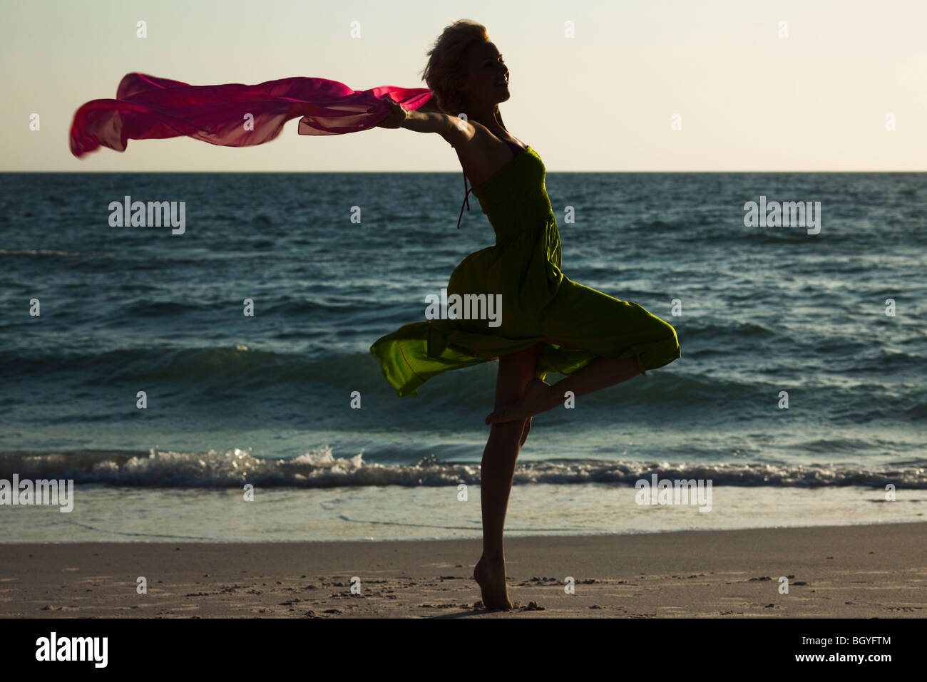 Woman at beach, balancing on one leg, holding scarf out in wind Stock ...