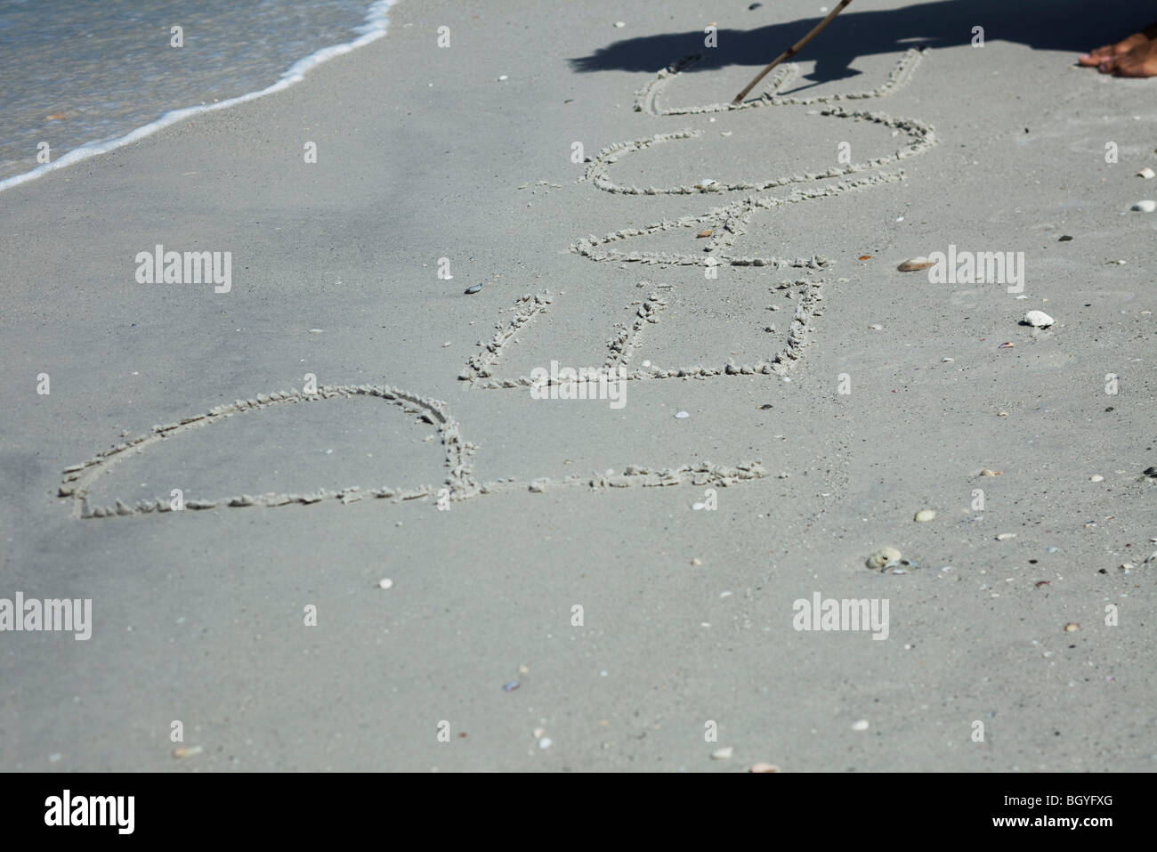 Person standing on beach, writing word "peace" in sand with stick ...