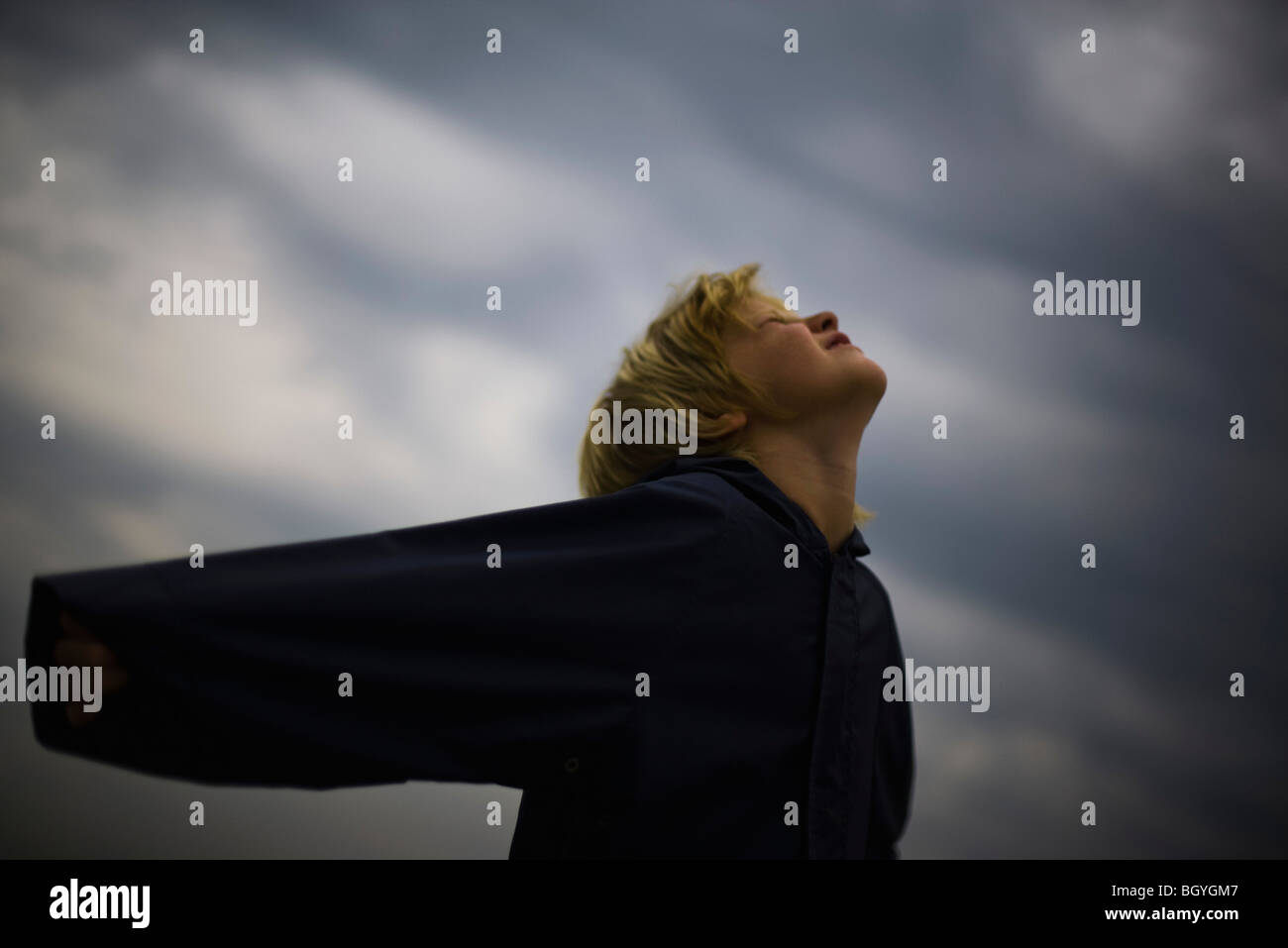 Boy with arms outstretched, head back, looking up at sky Stock Photo ...