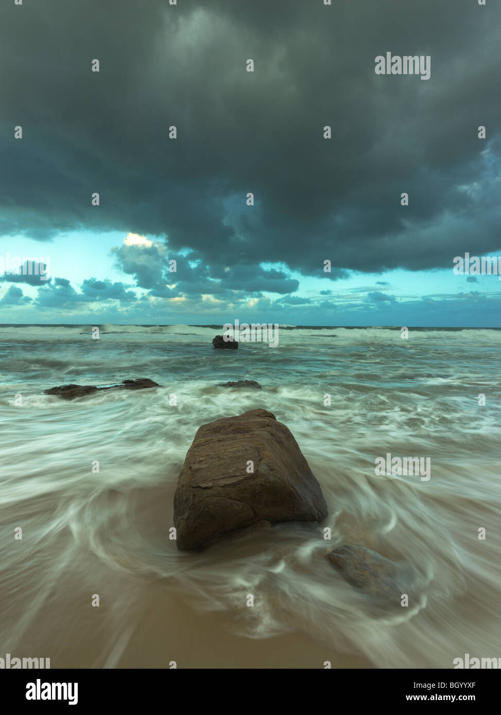 Immovable rock in a swirl of tide under a swirl of menacing clouds ...