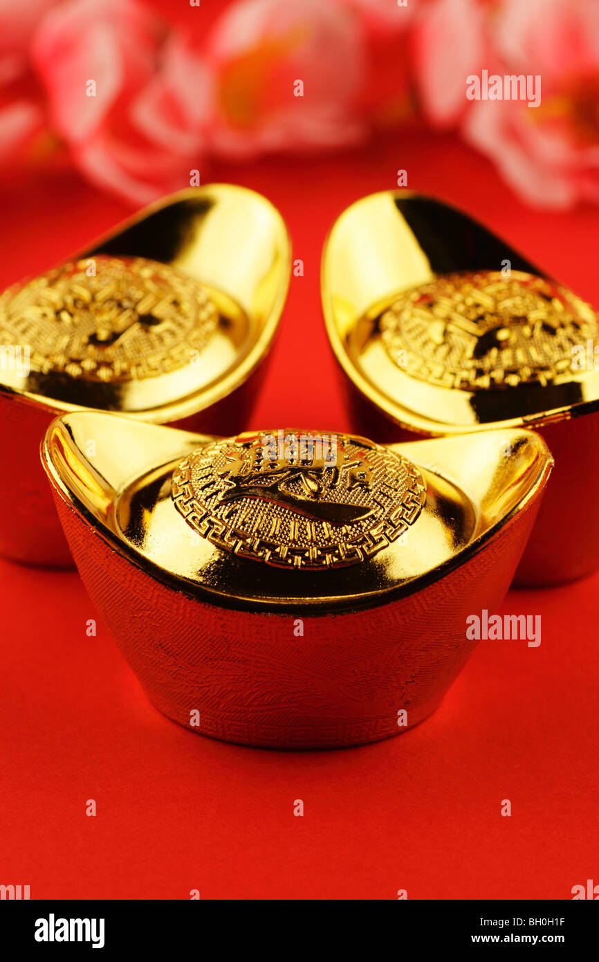 A trio of chinese gold ingots on a red background with some cherry ...