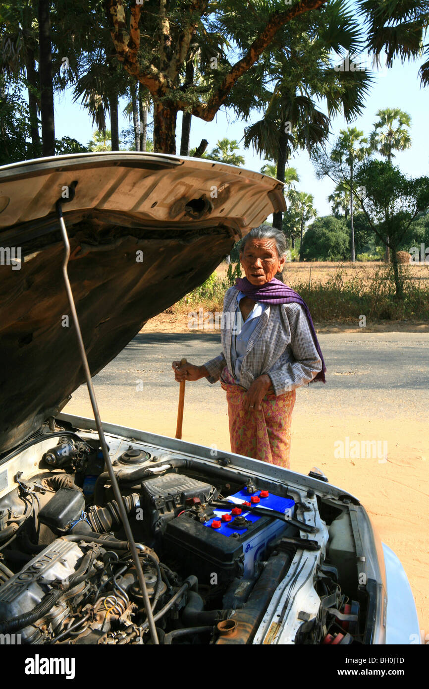 Old woman standing behind open bonnet on a country road, Myanmar, Burma ...