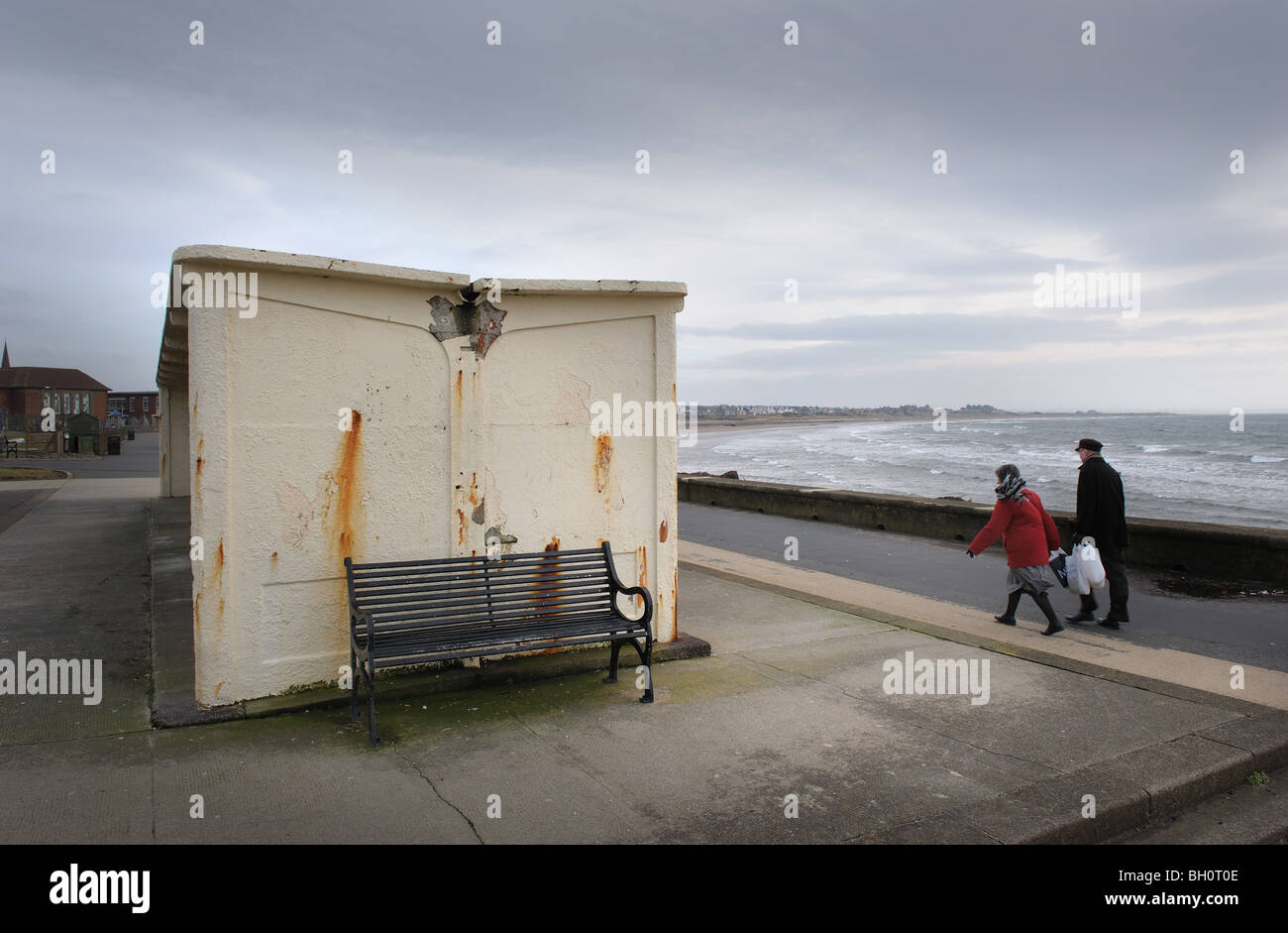 A couple walk home with shopping on a windy day along Esplanade, Troon ...