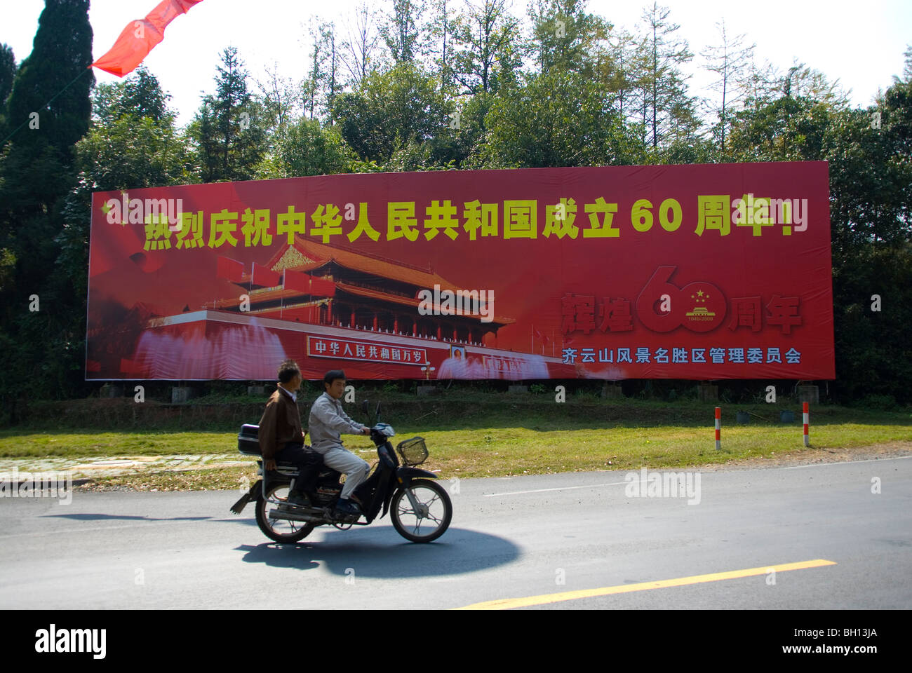 Two people on motorcycle passing a billboard of 60th anniversary of the ...