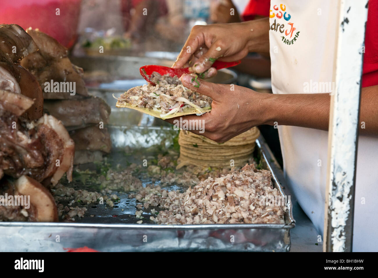 hands of a man making pork tacos at a street stall with one taco in ...