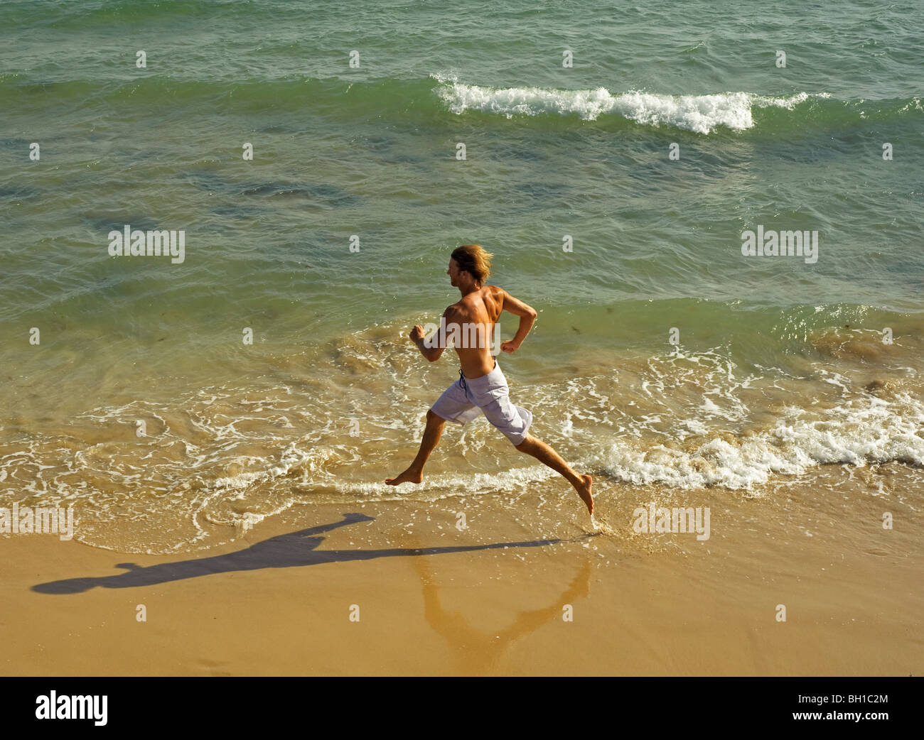 Young man running into water from beach Stock Photo - Alamy