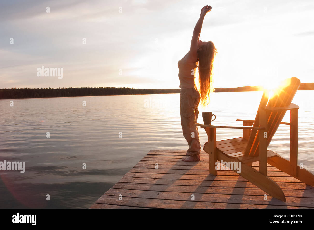 Woman reaching upward on dock at sunset, Clear Lake, Manitoba, Canada ...
