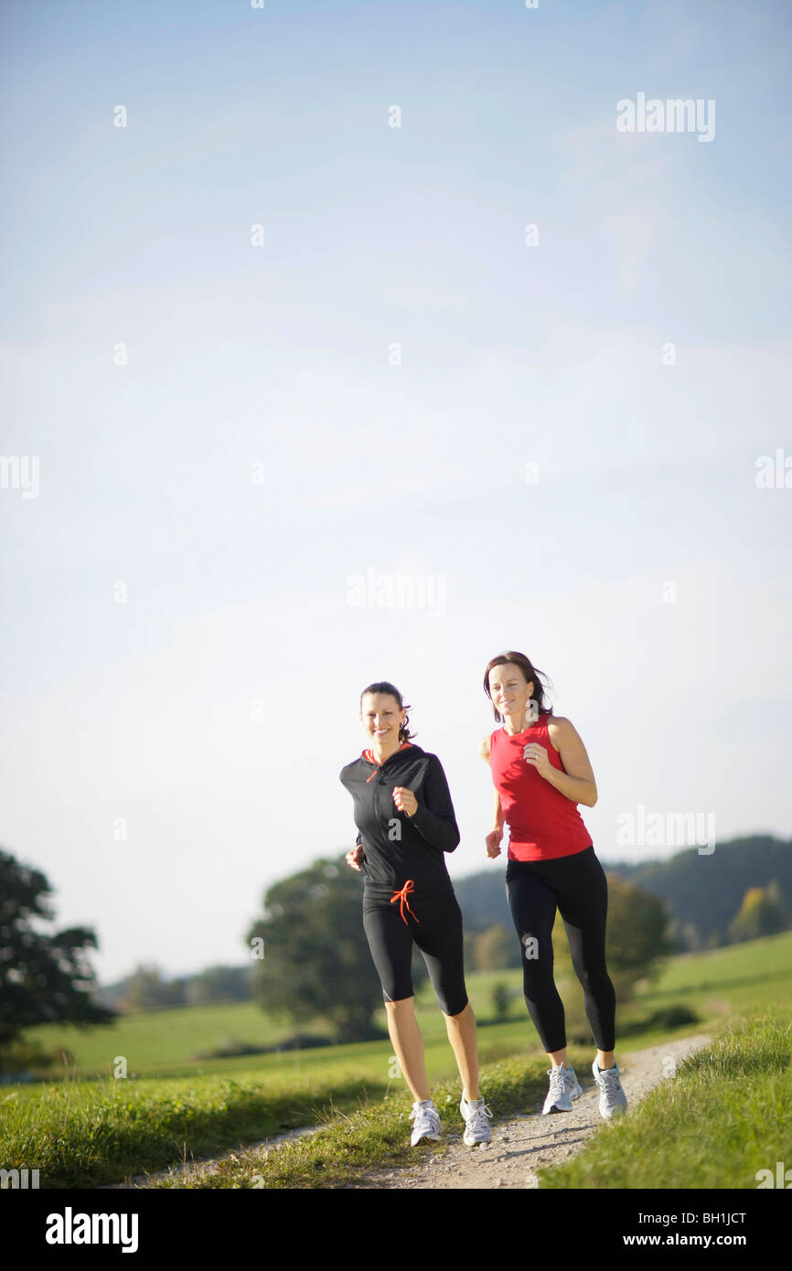 Two women running along dirt road, Munsing, Bavaria, Germany Stock ...