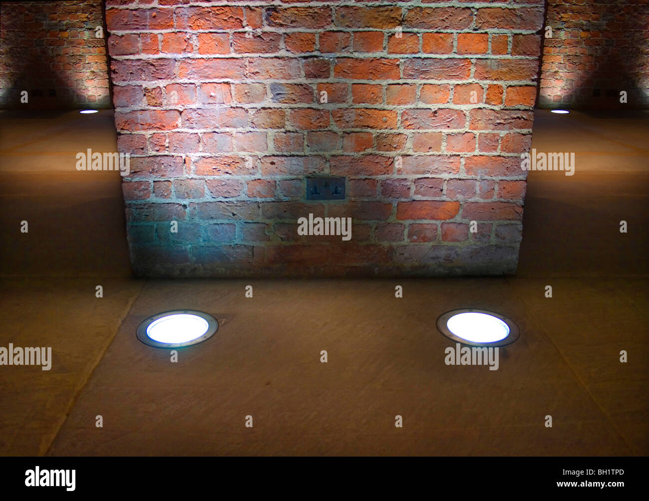 Two spotlights set in a stone floor light up a weathered brick wall ...