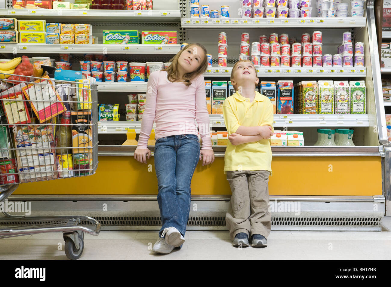 Brother and sister sit side by side on fridge counter in supermarket ...