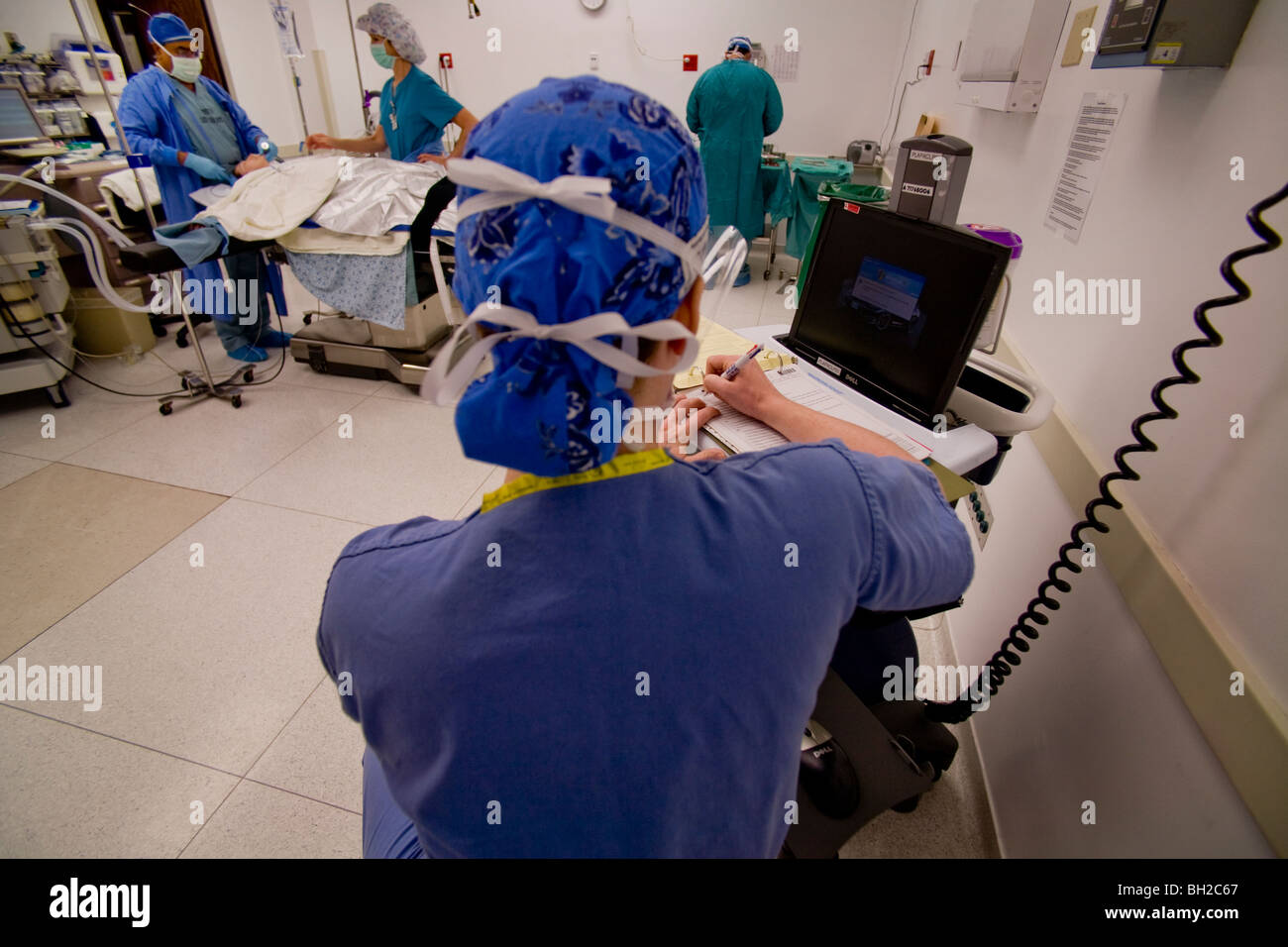 Dressed in "scrubs" and using a computer for a desk, a woman surgeon ...