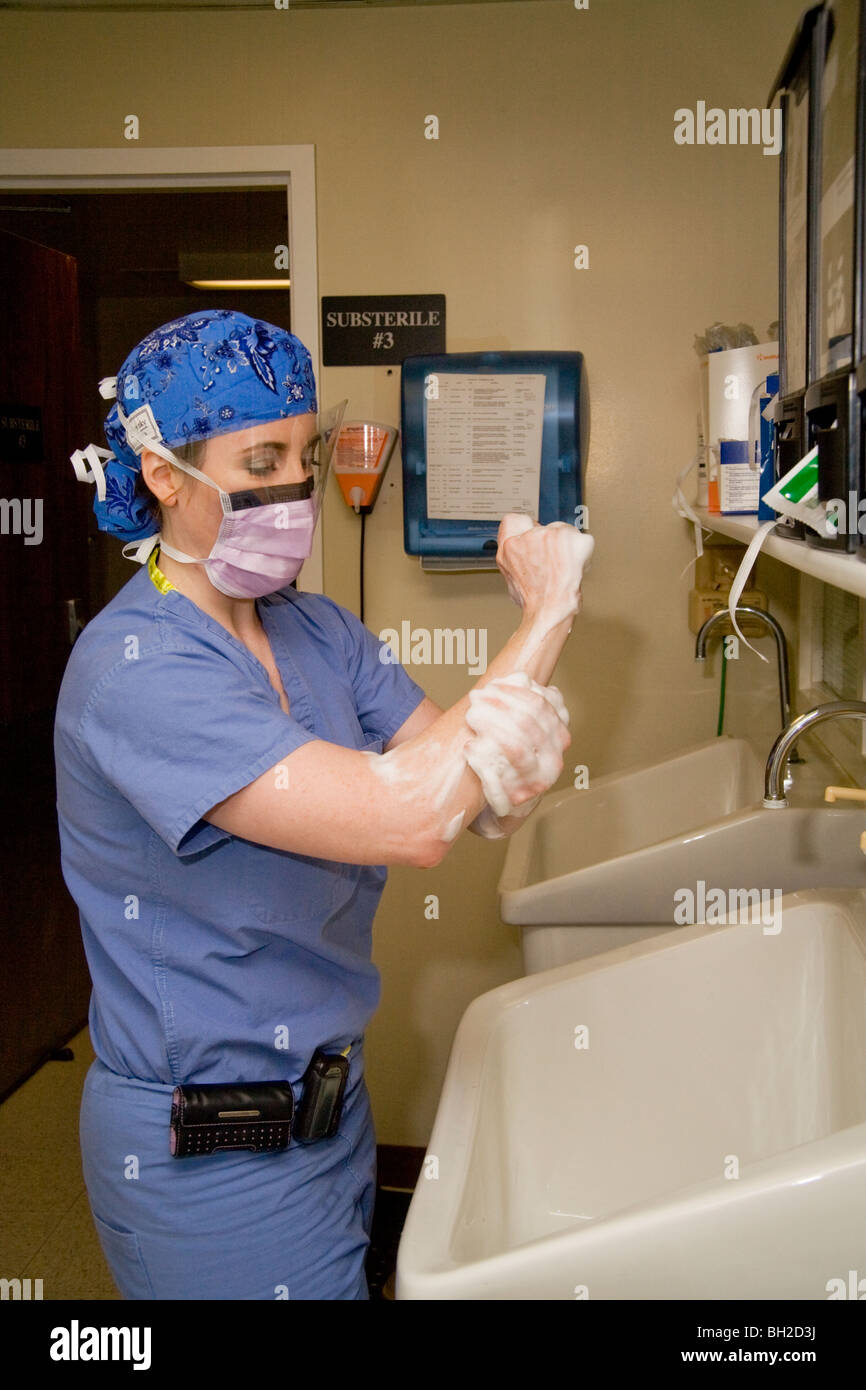 Dressed in "scrubs" and wearing a surgical mask, a woman surgeon washes ...