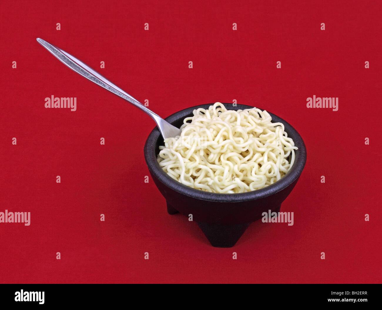 Noodles in black bowl against red background Stock Photo - Alamy
