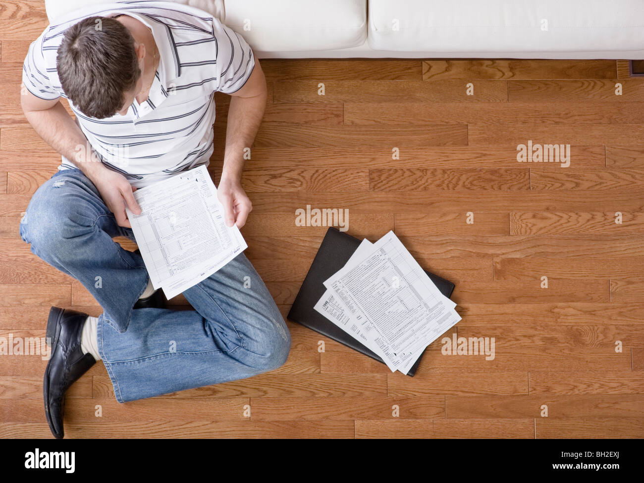 Young man sits on the floor as he looks through paperwork. Horizontal ...