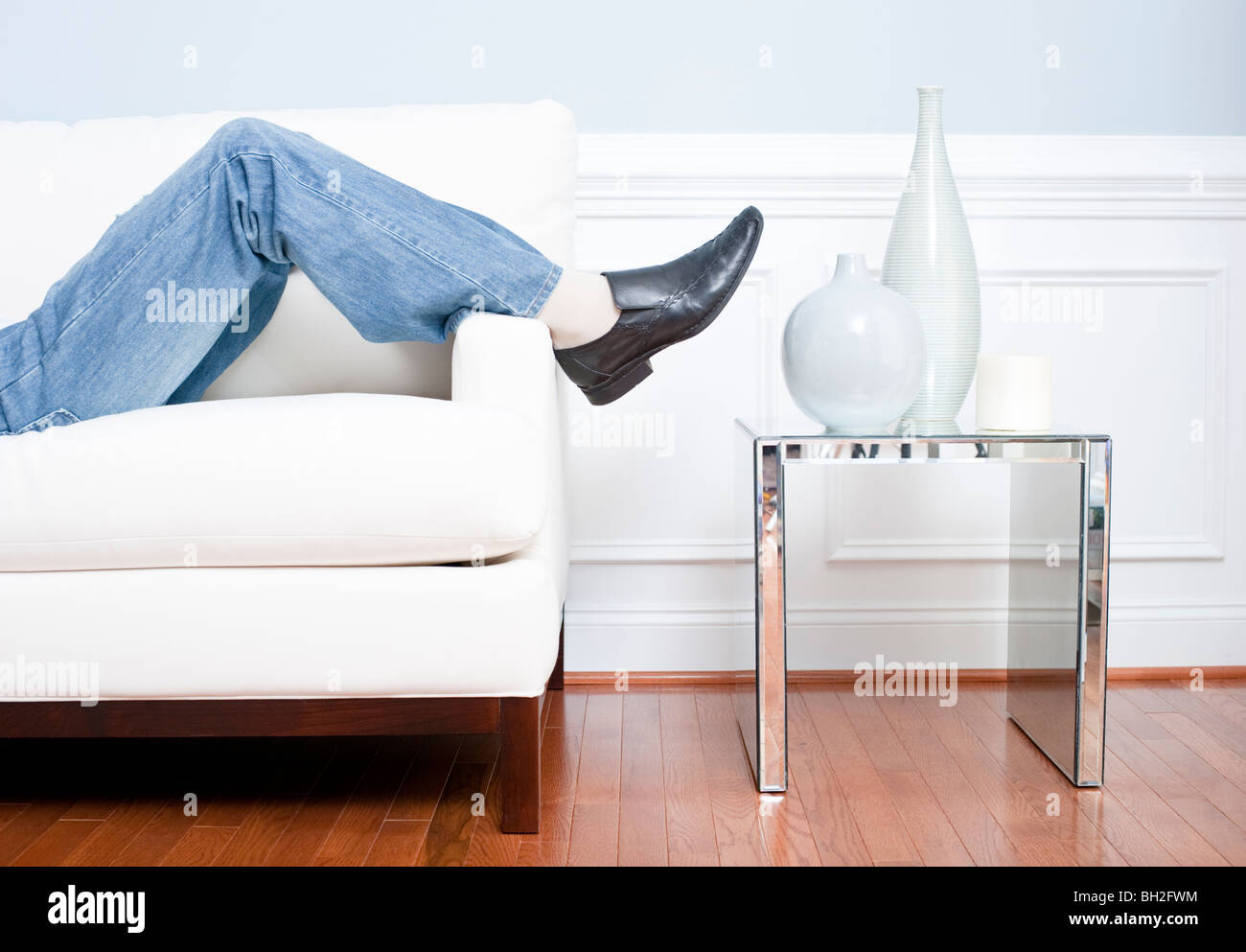 Cropped view of man reclining on white couch next to an end table ...