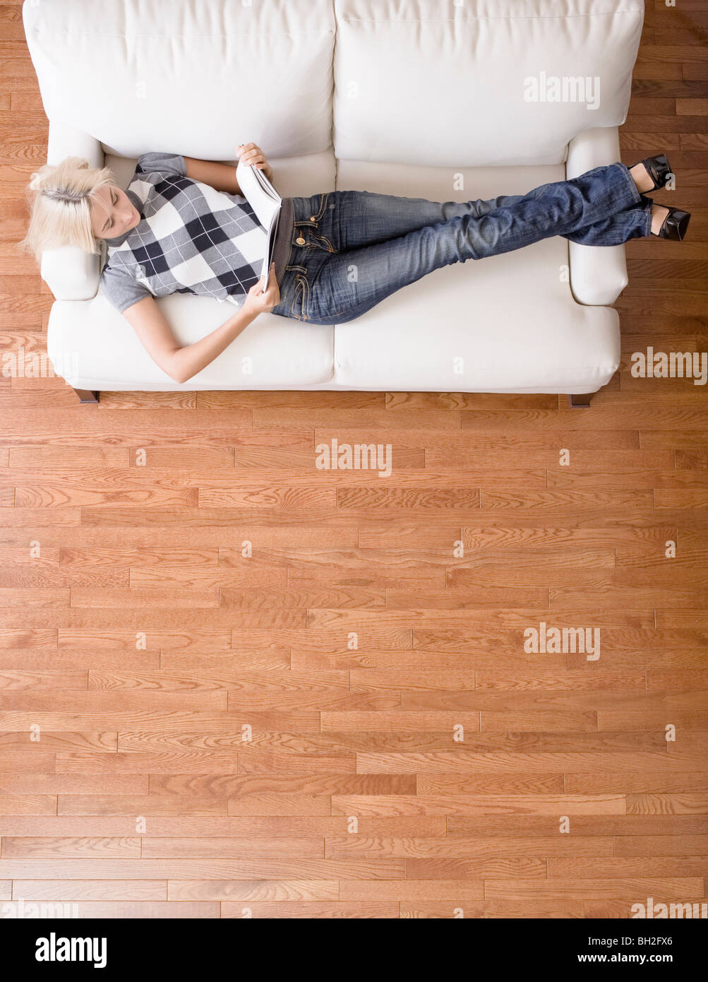 Full length overhead view of woman reclining and reading on white couch ...