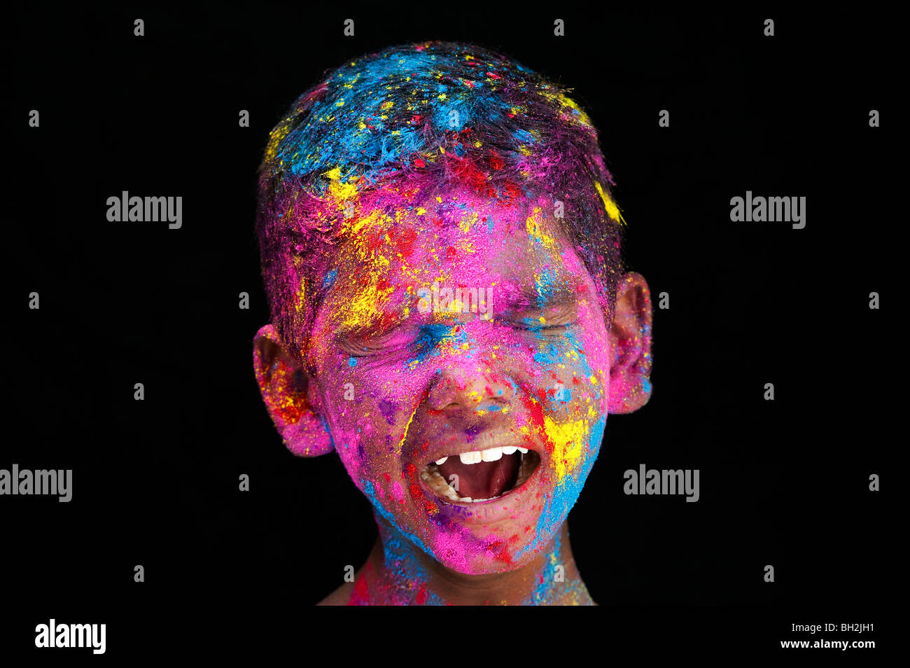 Young Indian boy crying with laughter whilst covered in coloured powder ...