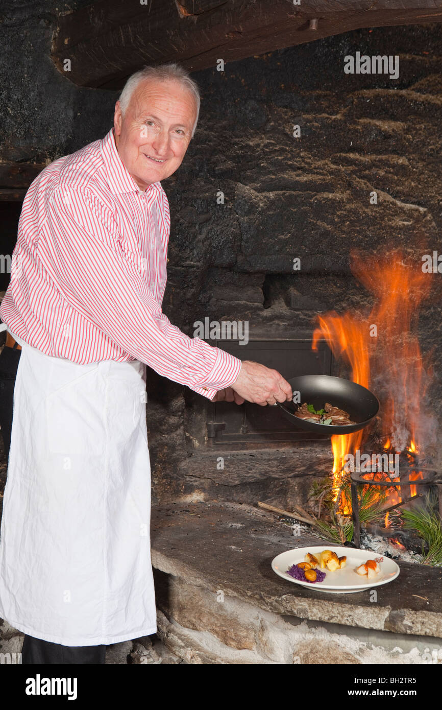 elderly cook by fireplace serving food Stock Photo - Alamy