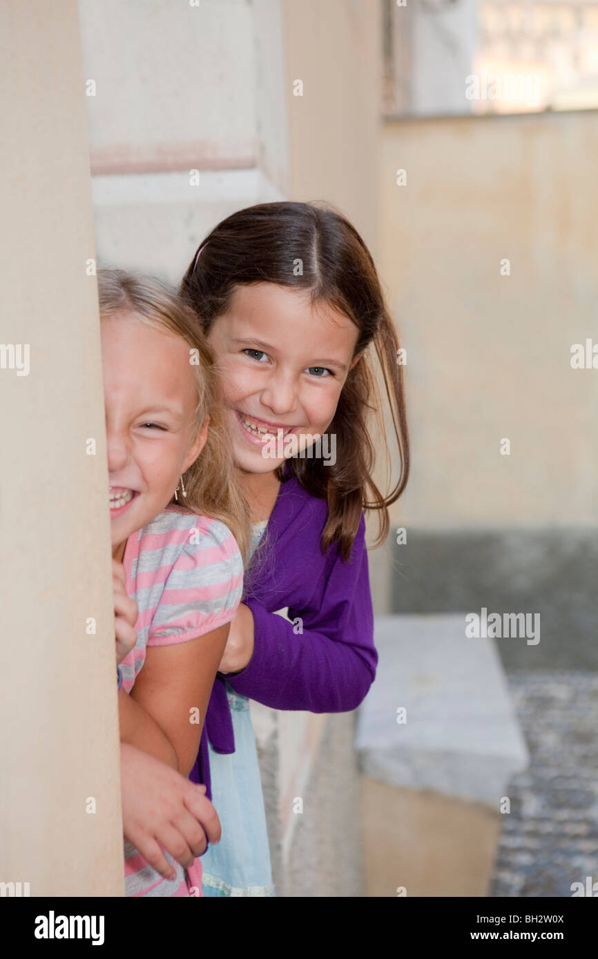 two girls hiding behind wall, laughing Stock Photo - Alamy