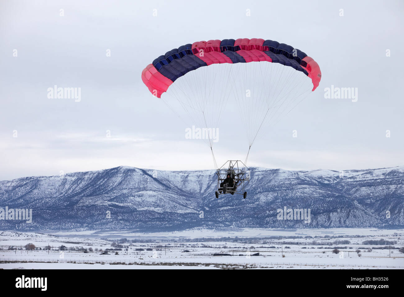 Powered parachute flying a low approach over snow covered winter valley ...