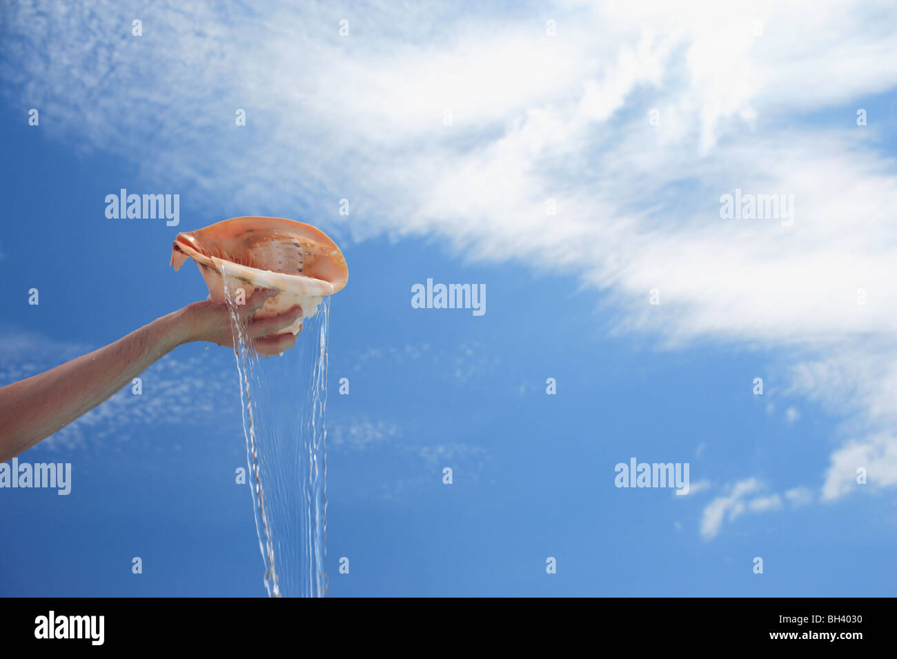 Man's hand pouring water from a large sea shell in the air against a ...